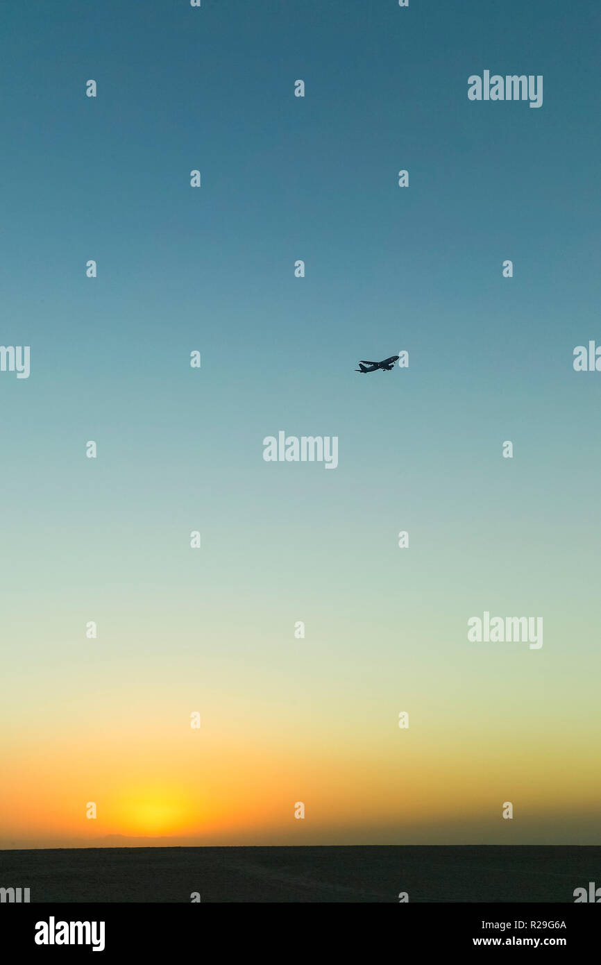 A passenger jet airplane soars over the Pacific Ocean at sunset along ...