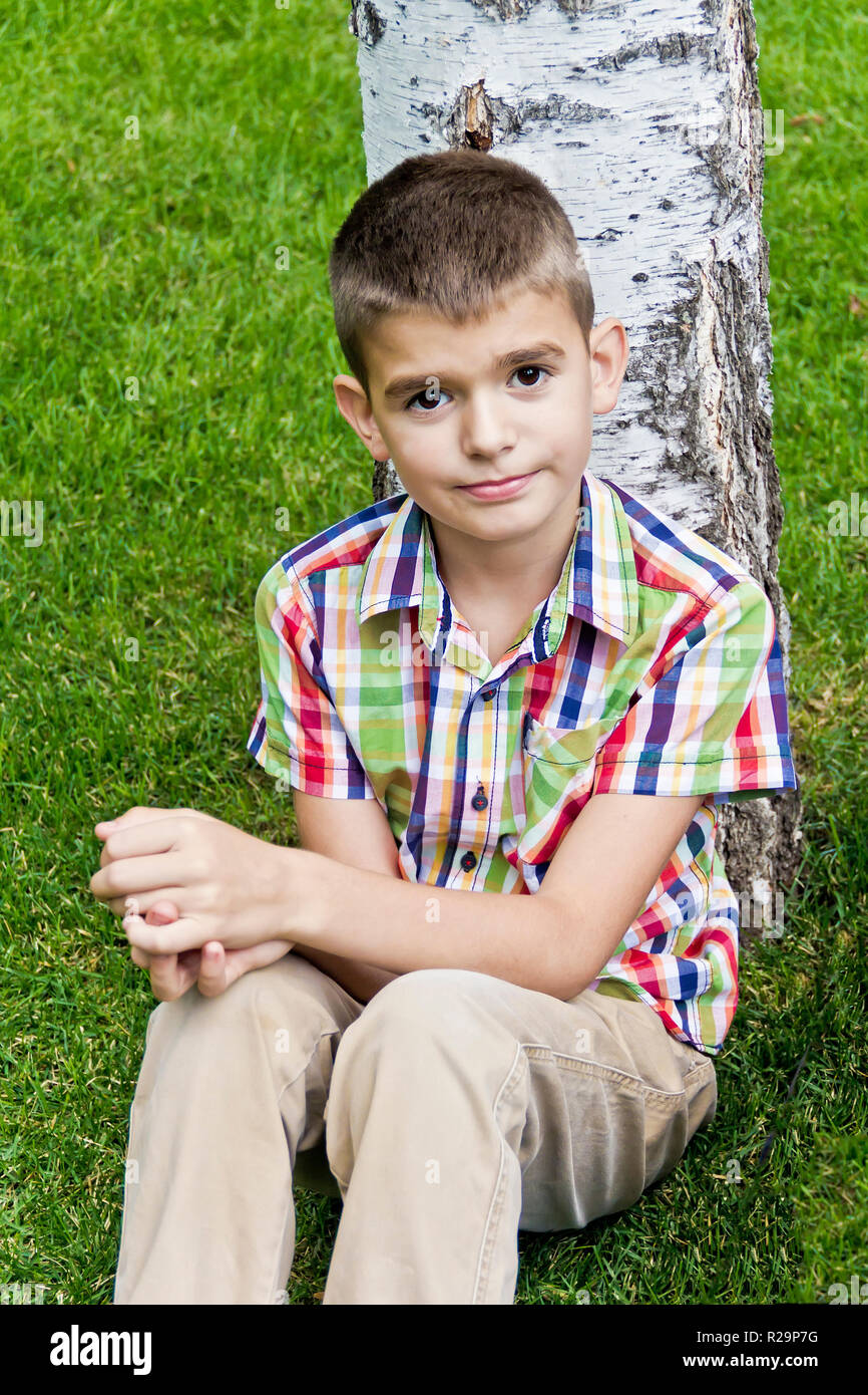 Cute brunette boy eleven years old sitting near tree Stock Photo - Alamy