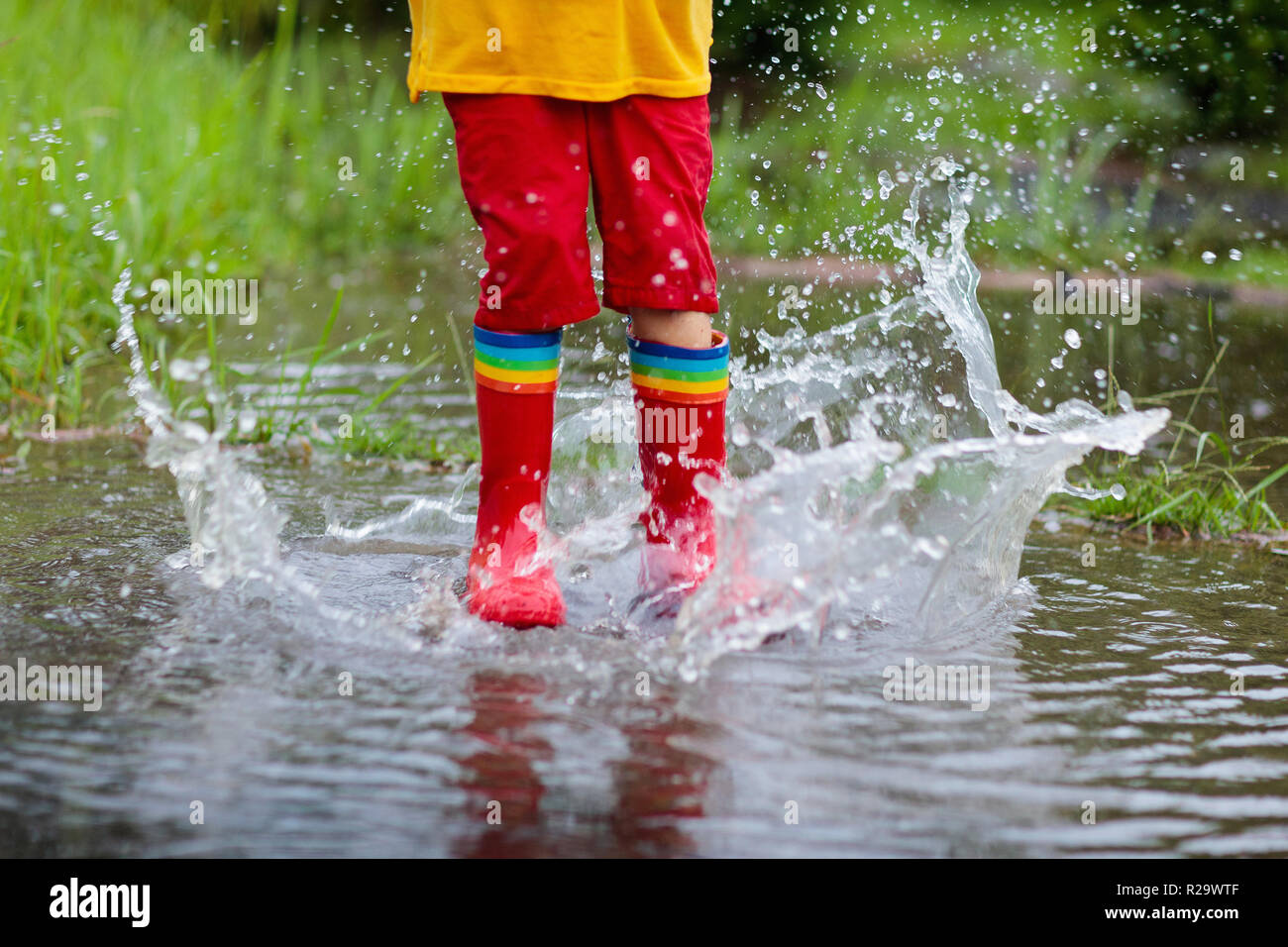 Kid playing out in the rain. Children with umbrella and rain boots play ...