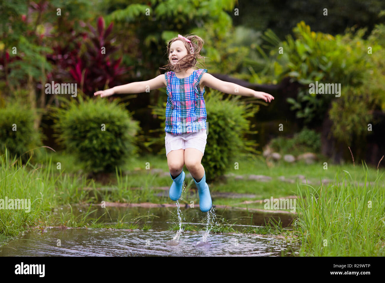 Kid playing out in the rain. Children with umbrella and rain boots play ...