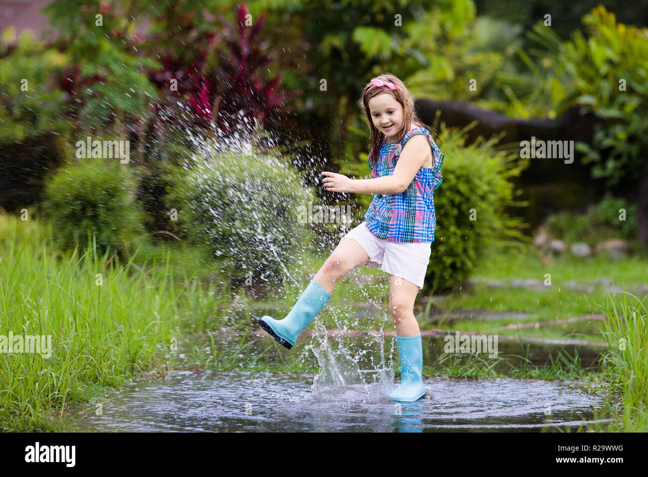 Kid playing out in the rain. Children with umbrella and rain boots play ...