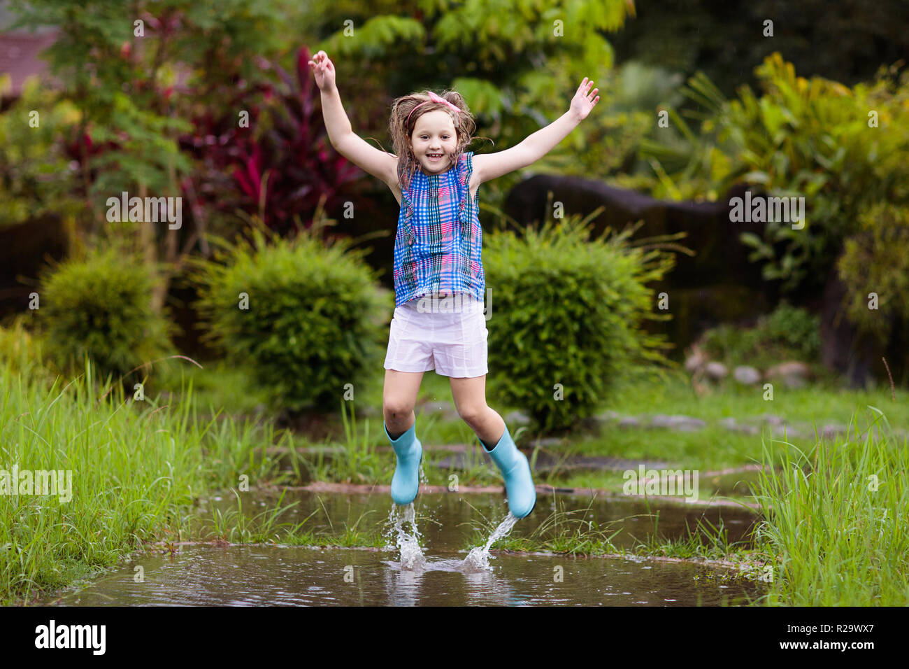 Kid playing out in the rain. Children with umbrella and rain boots play ...