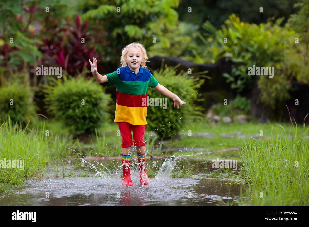 Kid playing out in the rain. Children with umbrella and rain boots play ...