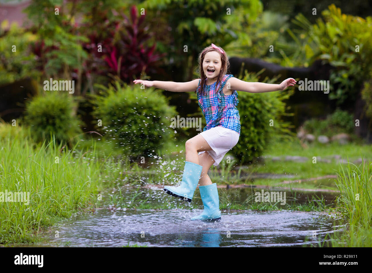 Kid playing out in the rain. Children with umbrella and rain boots play ...