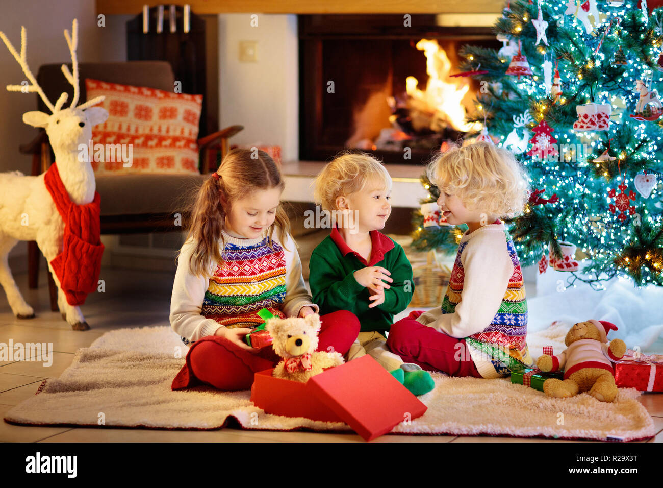 Children at Christmas tree and fireplace on Xmas eve. Family with kids ...