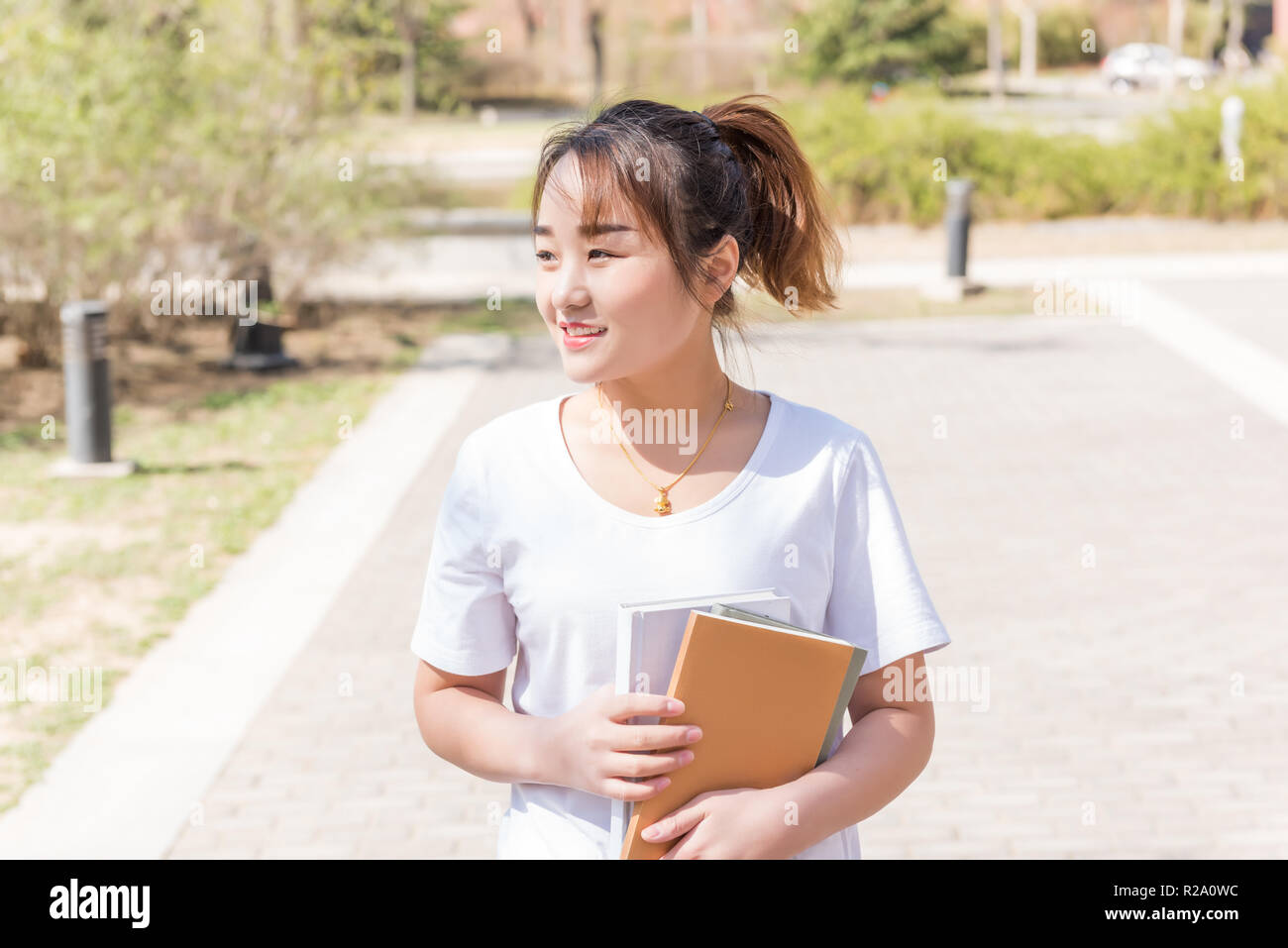 Female university college student holding books with campus background ...