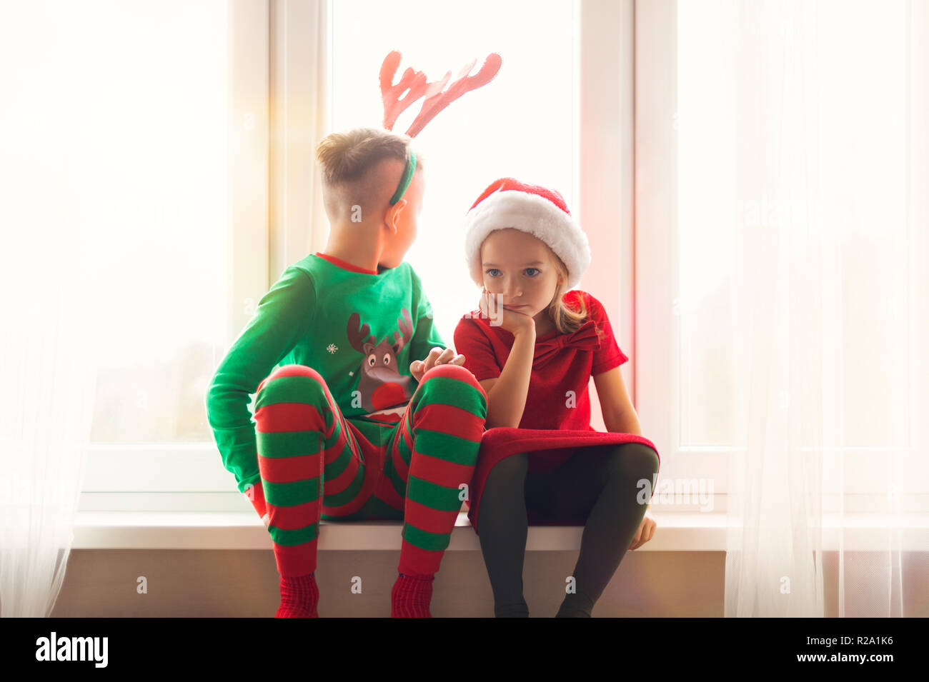 Brother and sister sitting restless on window sill at christmas time ...