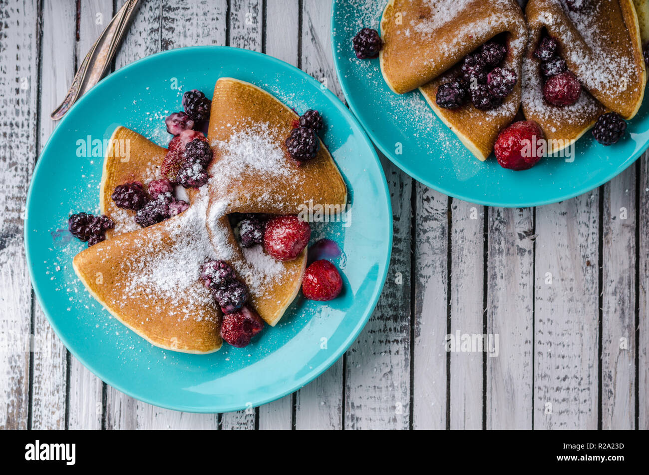Homemade crepes with frozen berries, topped sugar, rustic wood board ...