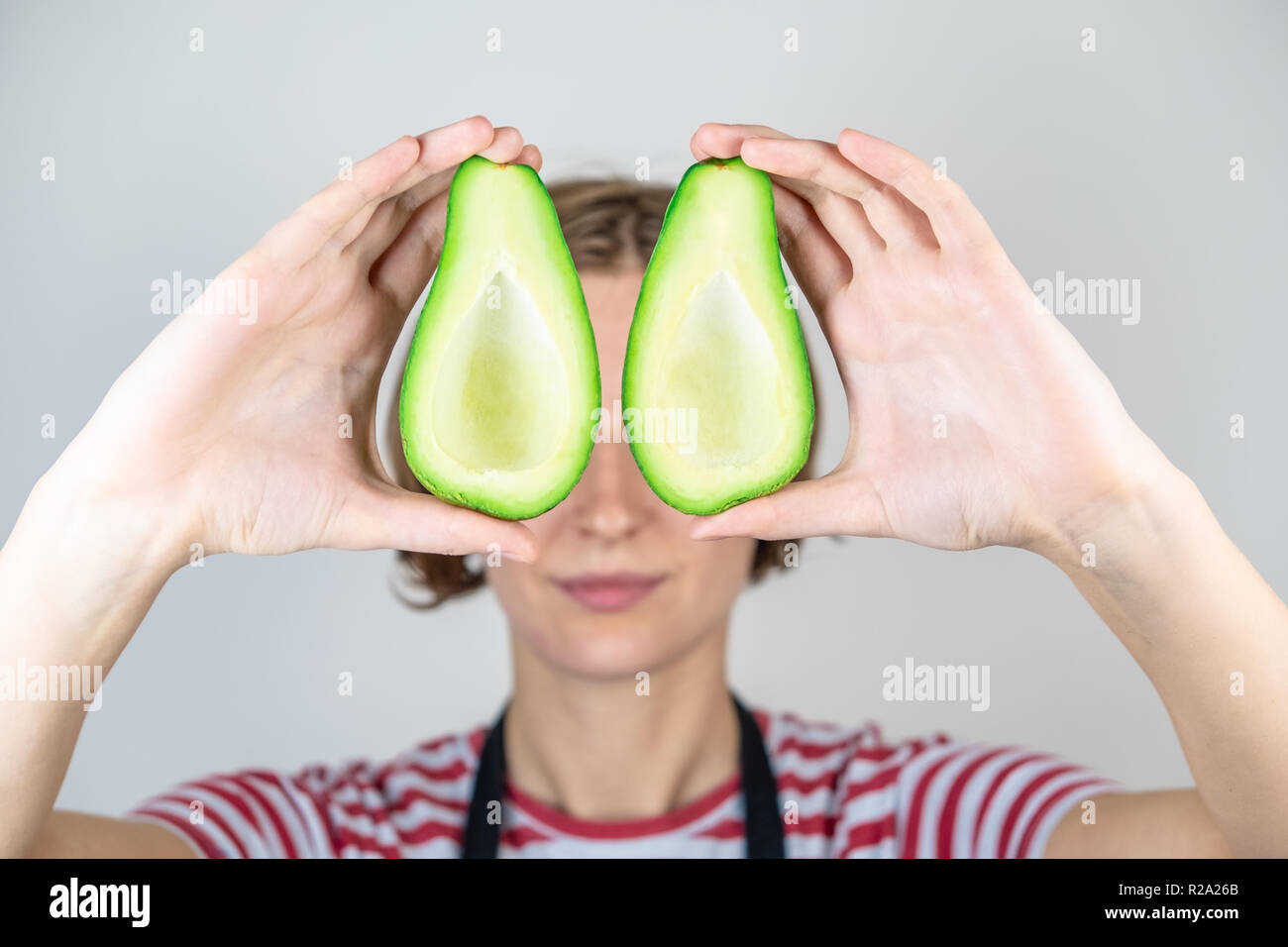 Fresh ripe avocado in woman hands. Female face hidden behind halves of ...