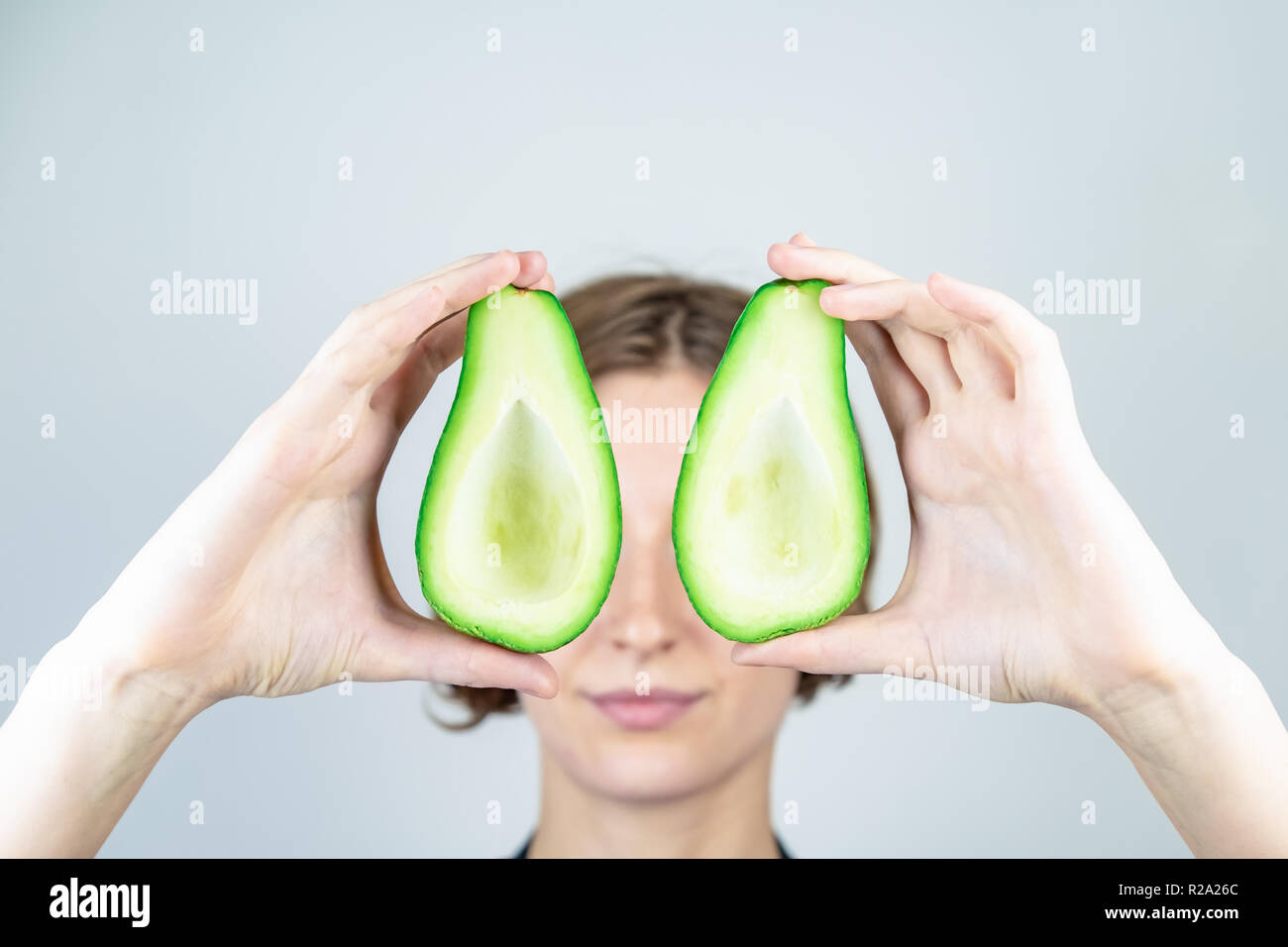 Fresh ripe avocado in woman hands. Female face hidden behind halves of ...