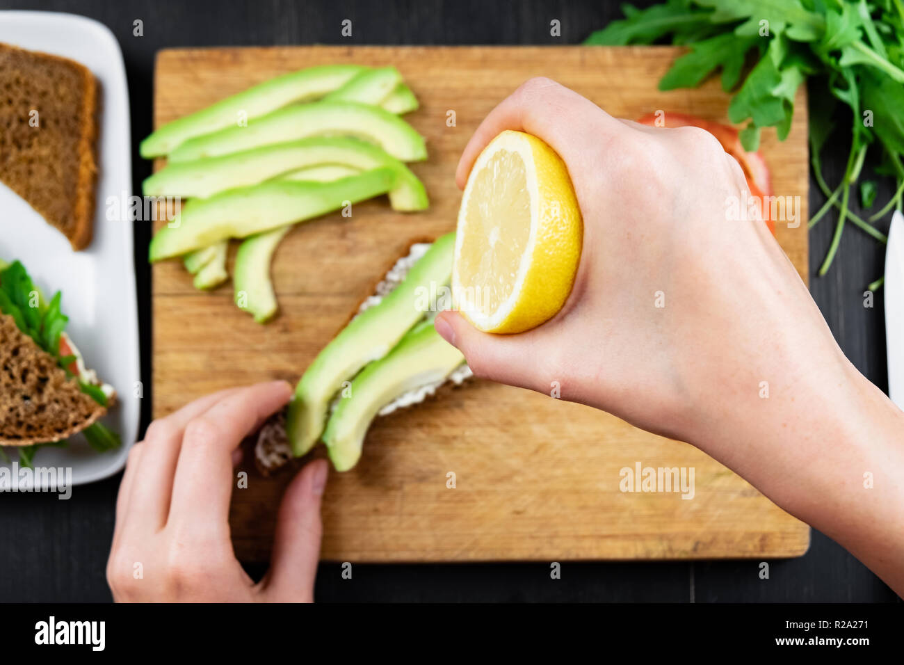 Making raw food snack. Female hands squeeze lemon juice onto avocado ...