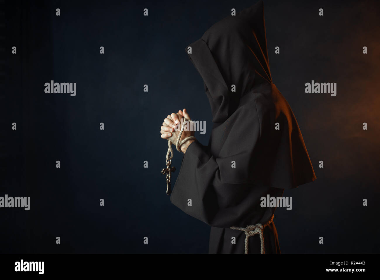 Medieval monk in black robe with hood praying with closed eyes, secret ...