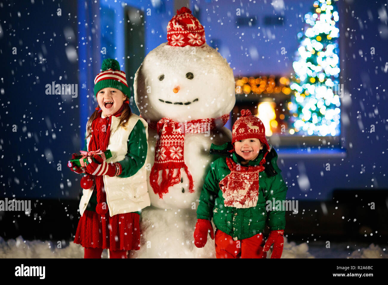 Kids build snowman on Christmas eve. Children in snowy backyard next to ...
