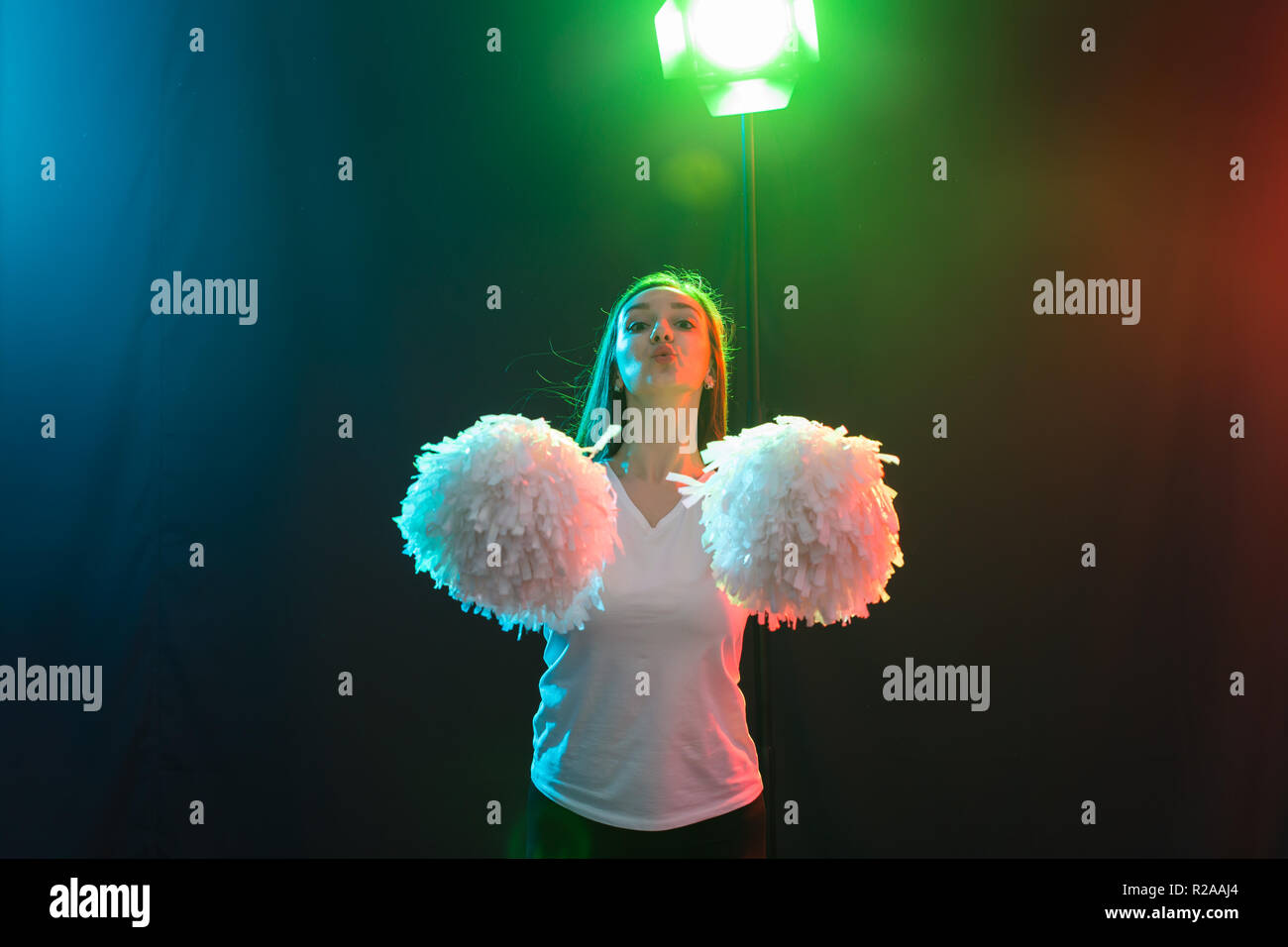 Cheerleading young woman dancing with pom-poms on colourful background ...