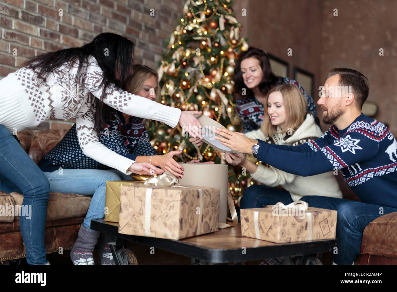 Young people opening Christmas gift boxes by a Christmas tree Stock ...