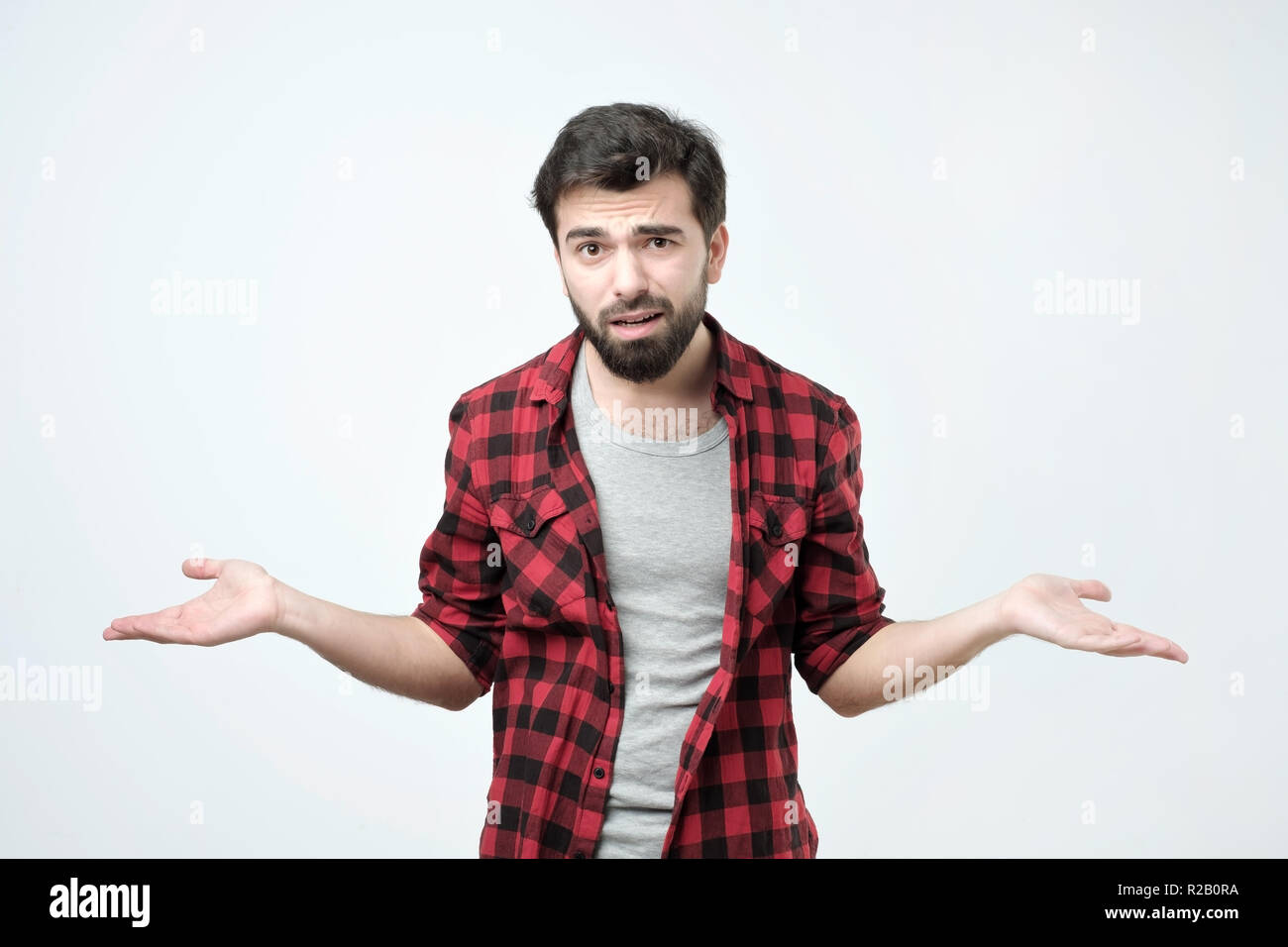 Confused young man dressed in black red shirt standing over white ...