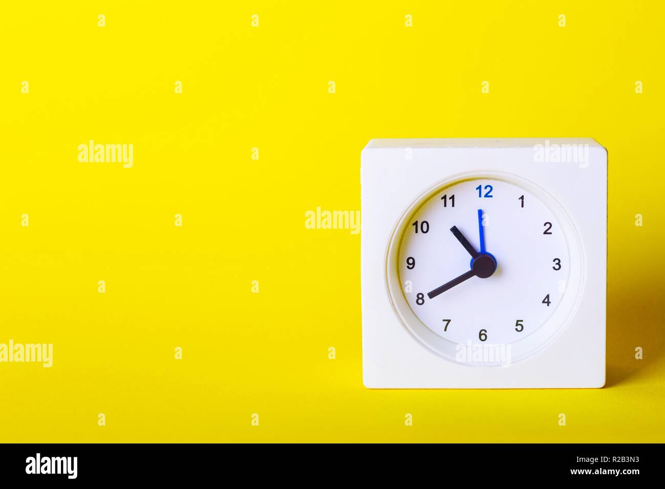 small square white clock on a yellow background Stock Photo - Alamy