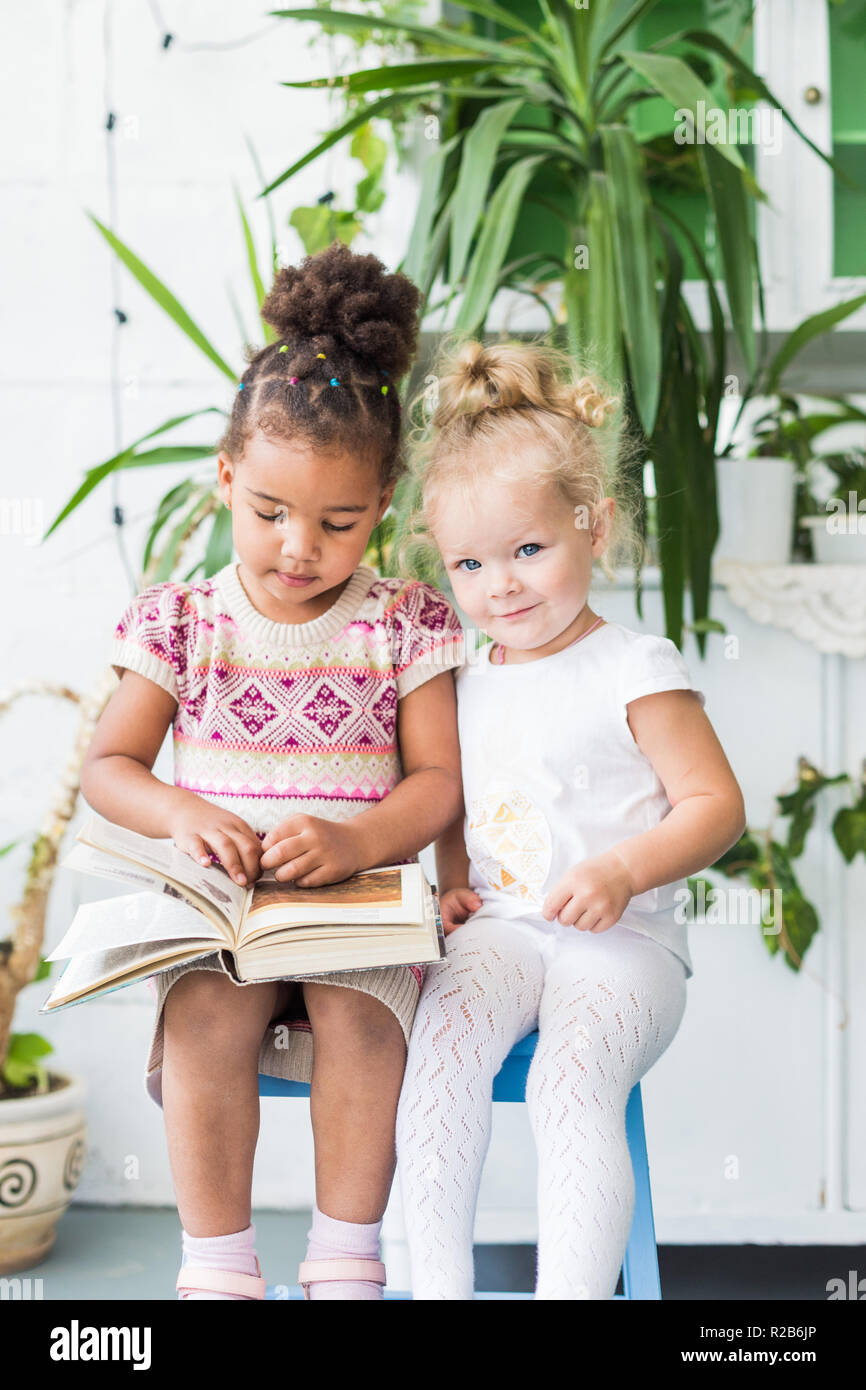 Two little girls read a book on the background of plants in pots Stock ...