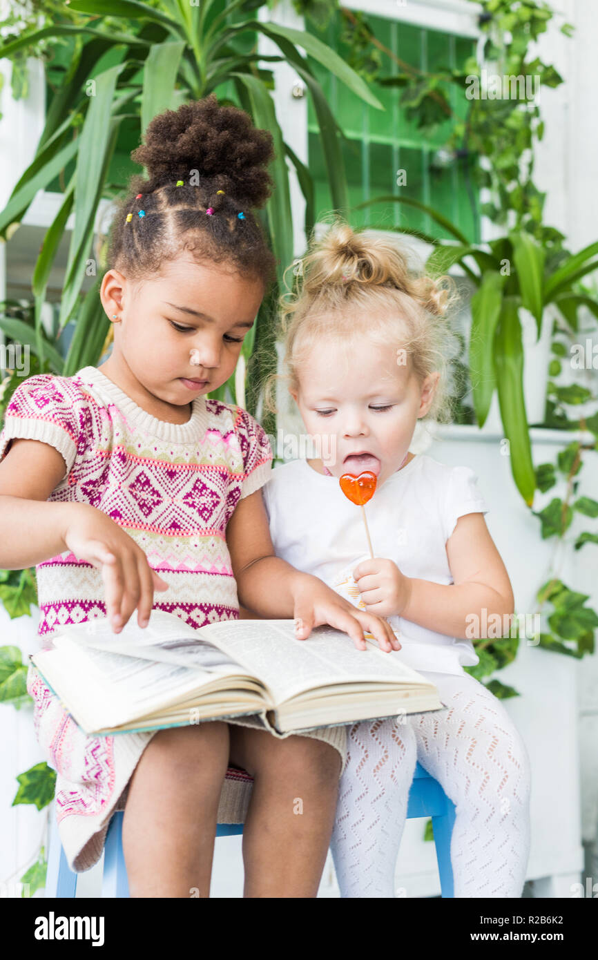 Two little girls read a book on the background of plants in pots Stock ...