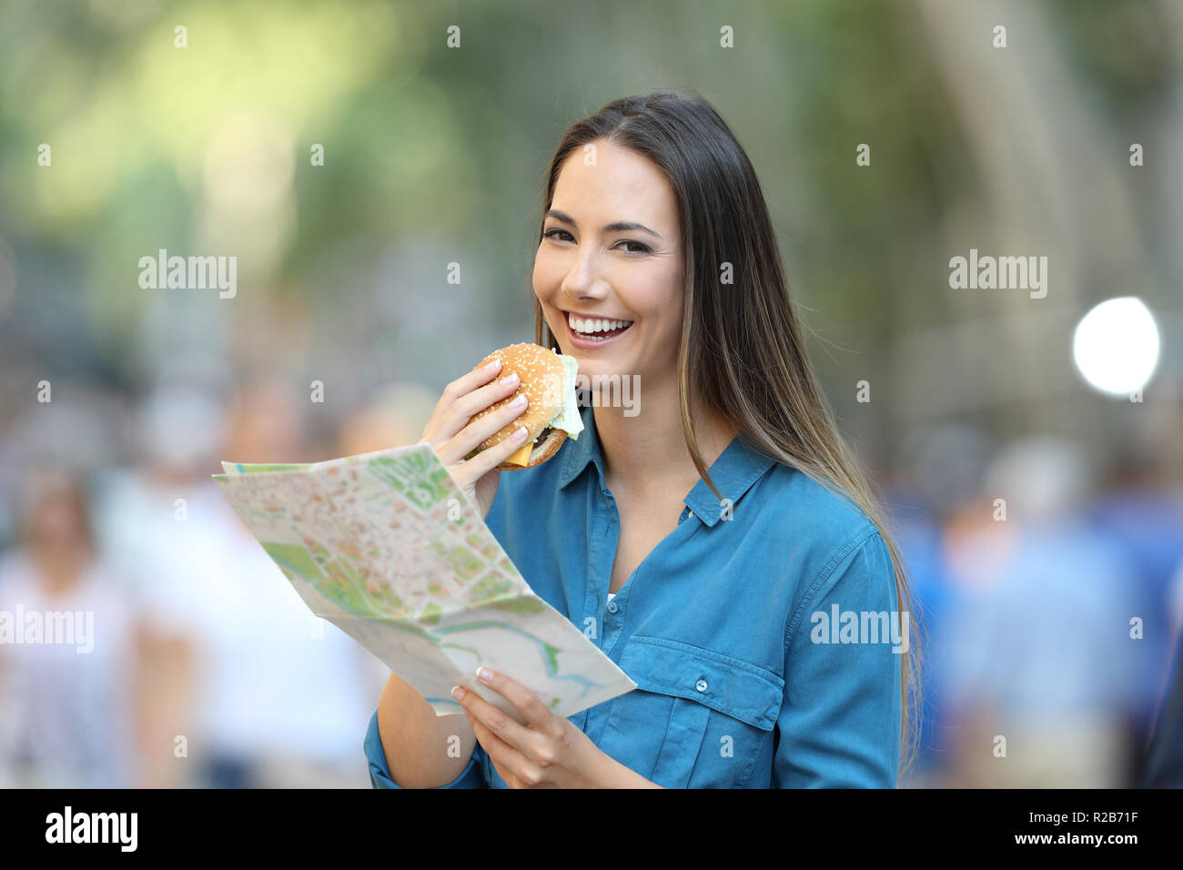 Happy tourist holding a paper map and a burger in the street Stock ...