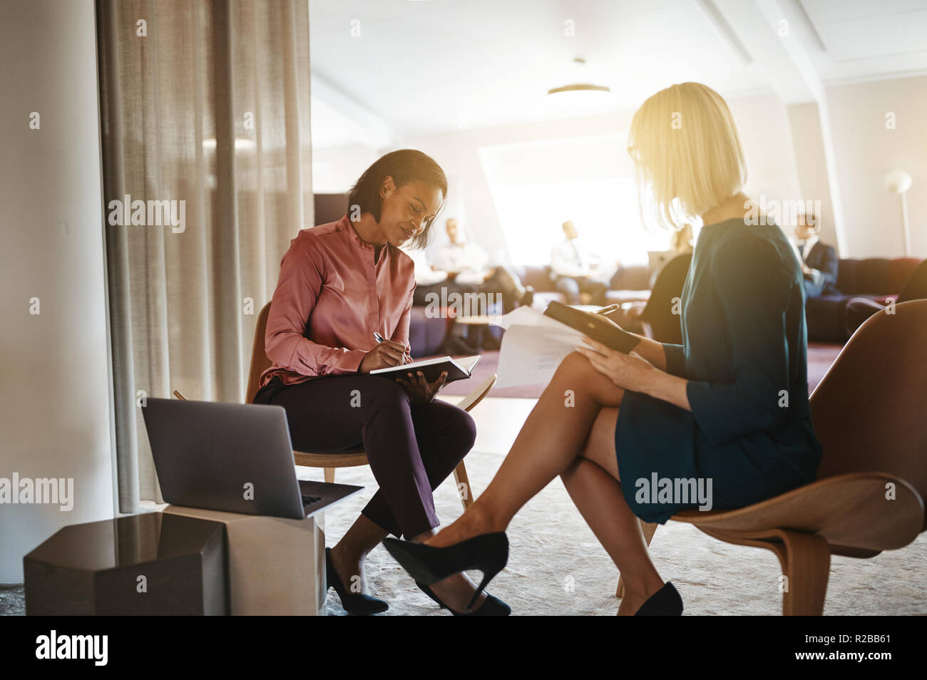 Two smiling female work colleagues sitting together in a bright modern ...