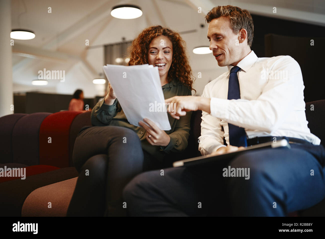 Two diverse work colleagues sitting on a sofa in a modern office ...