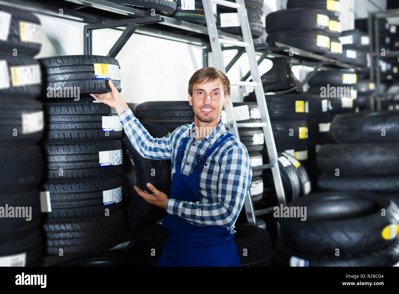 Young working man standing with new auto tires for in hands in shop ...