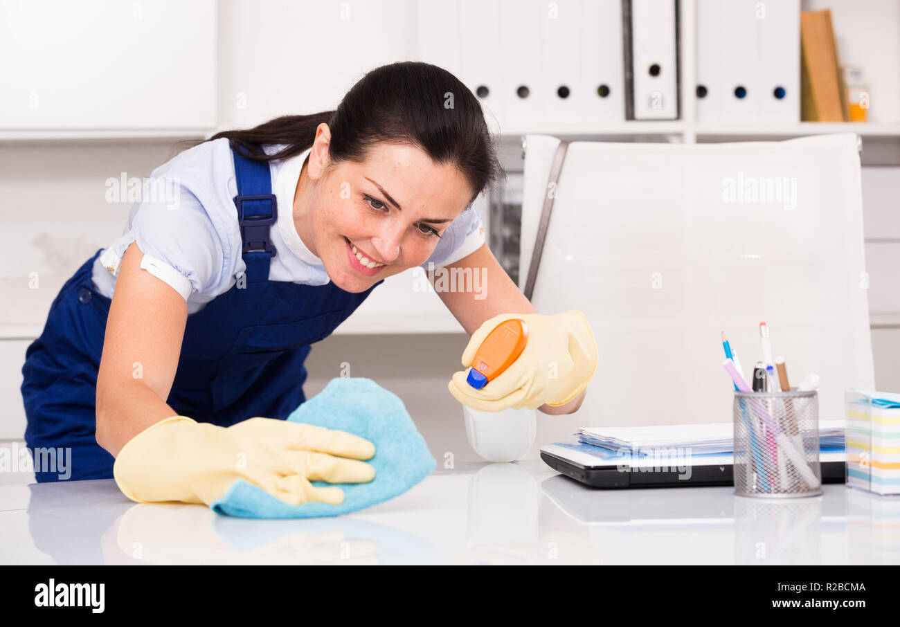 Portrait of adult female cleaning office table with rag and cleanser ...