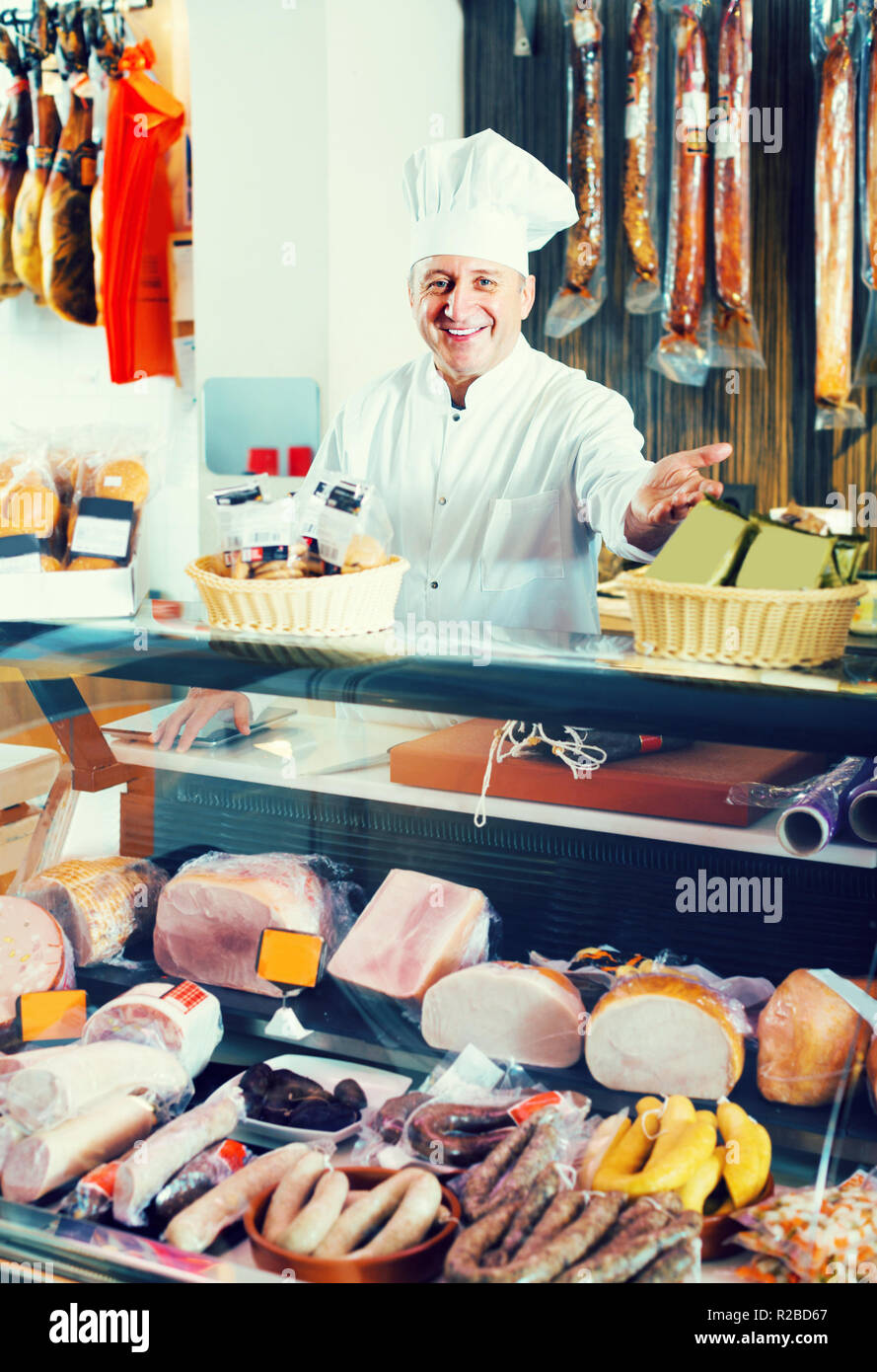 Mature male butcher with wurst, jamon and smoked meat at counter Stock ...