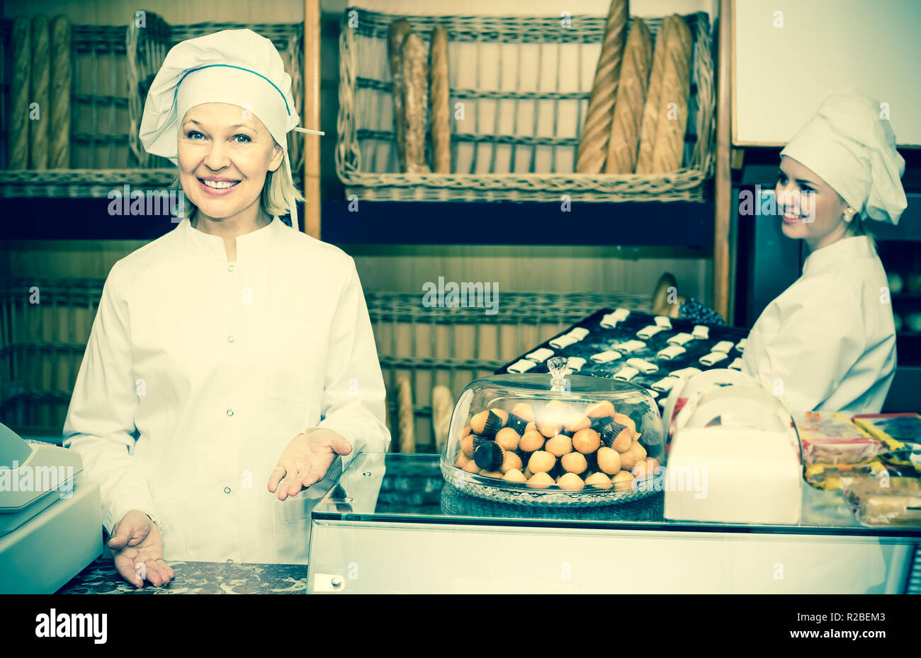 Portrait of two positive smiling female bakers with pastry in bakery ...