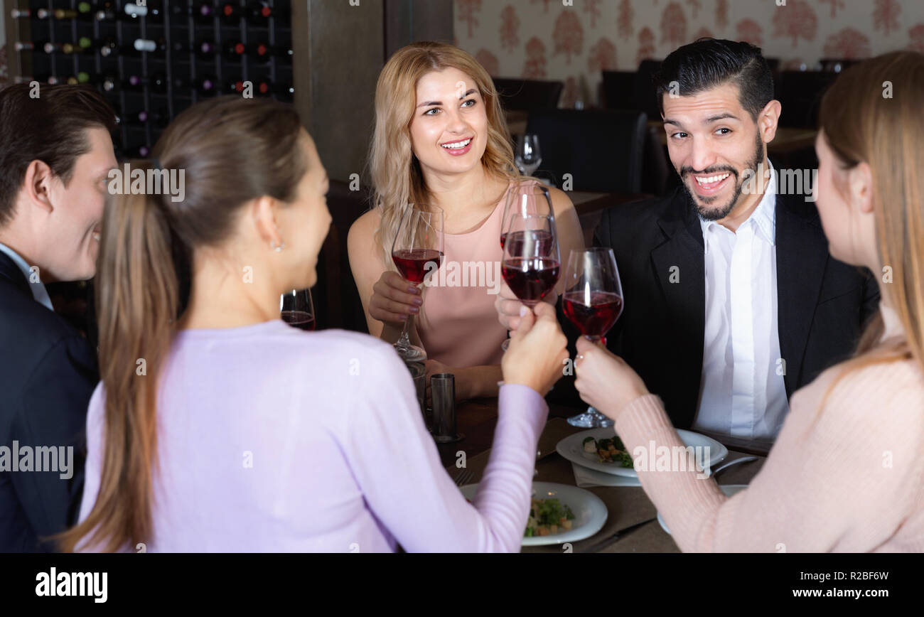 Сheerful smiling friends having dinner and drinking red wine in ...