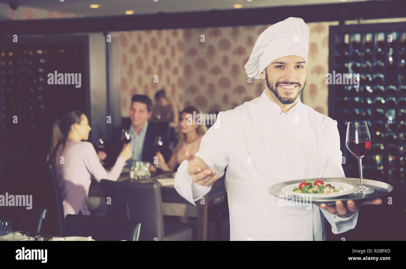 Handsome smiling male chef with dishes on serving tray welcoming to ...