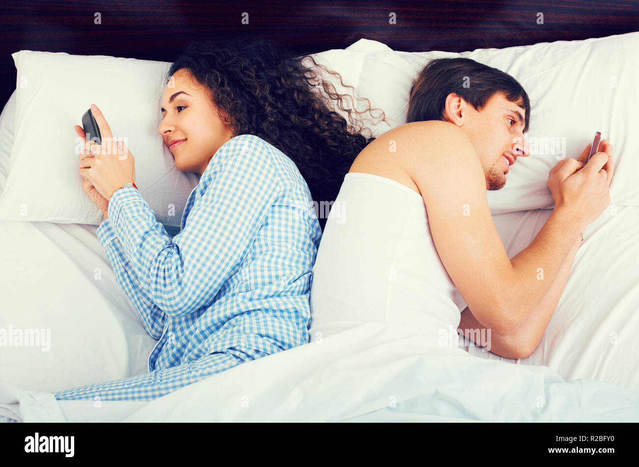 Young family couple in bed busy with mobile phones separately Stock ...