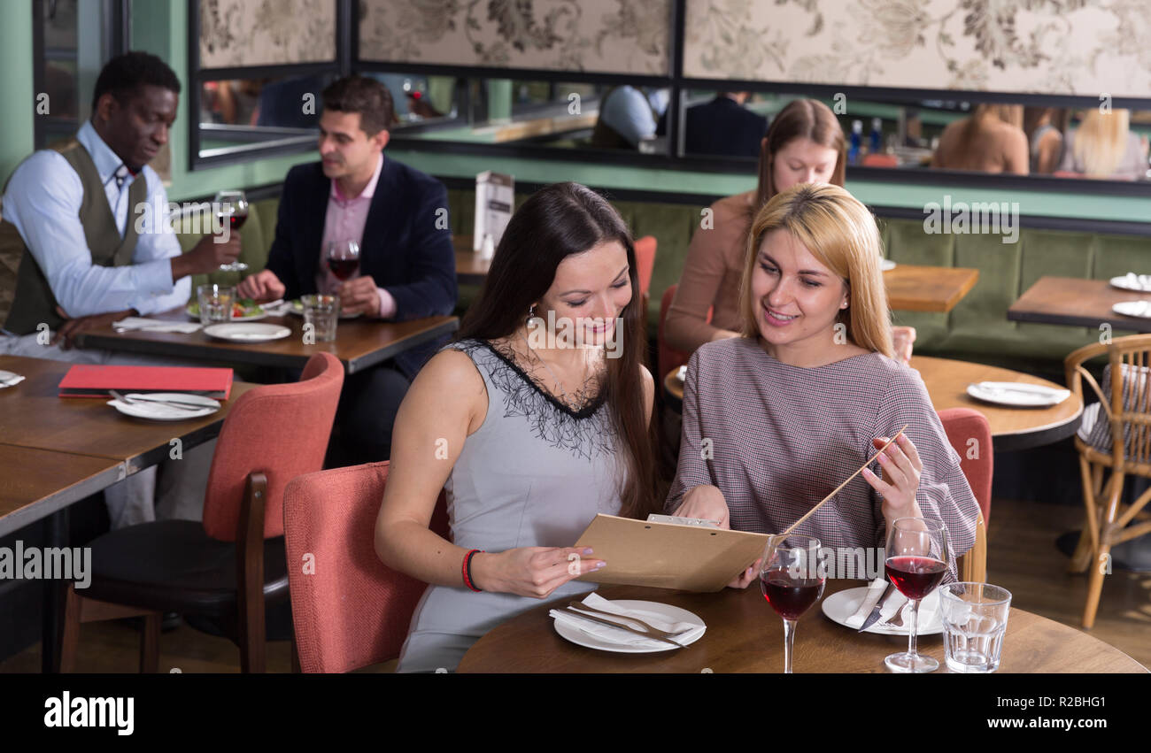 Two young attractive female friends choosing dishes from menu card in ...