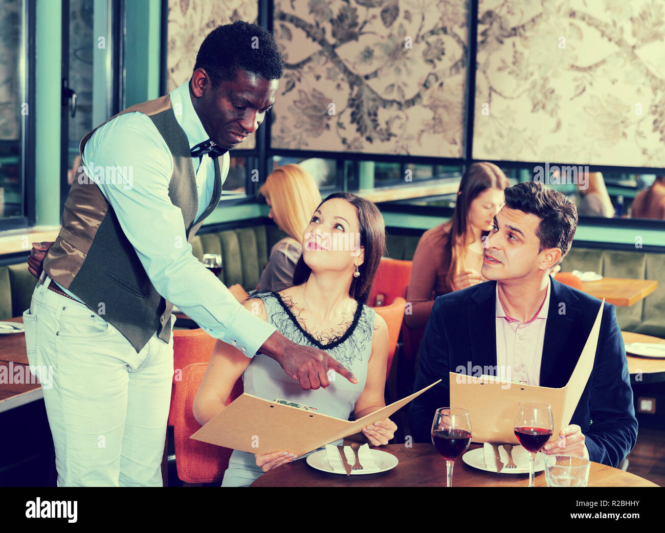 Smiling African American waiter taking order from couple, recommending ...