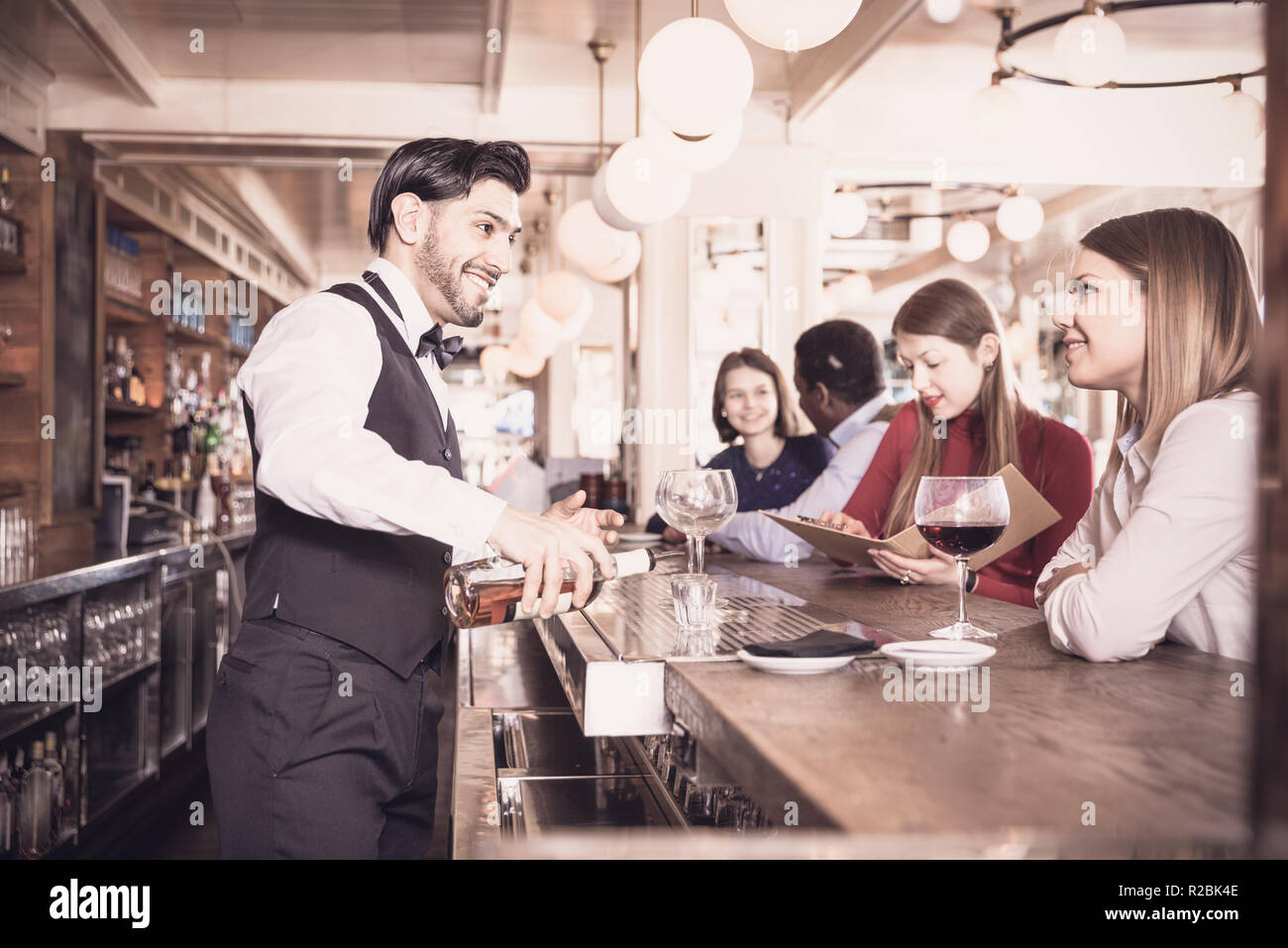 Cheerful positive barman is servicing young people who are relaxing in ...