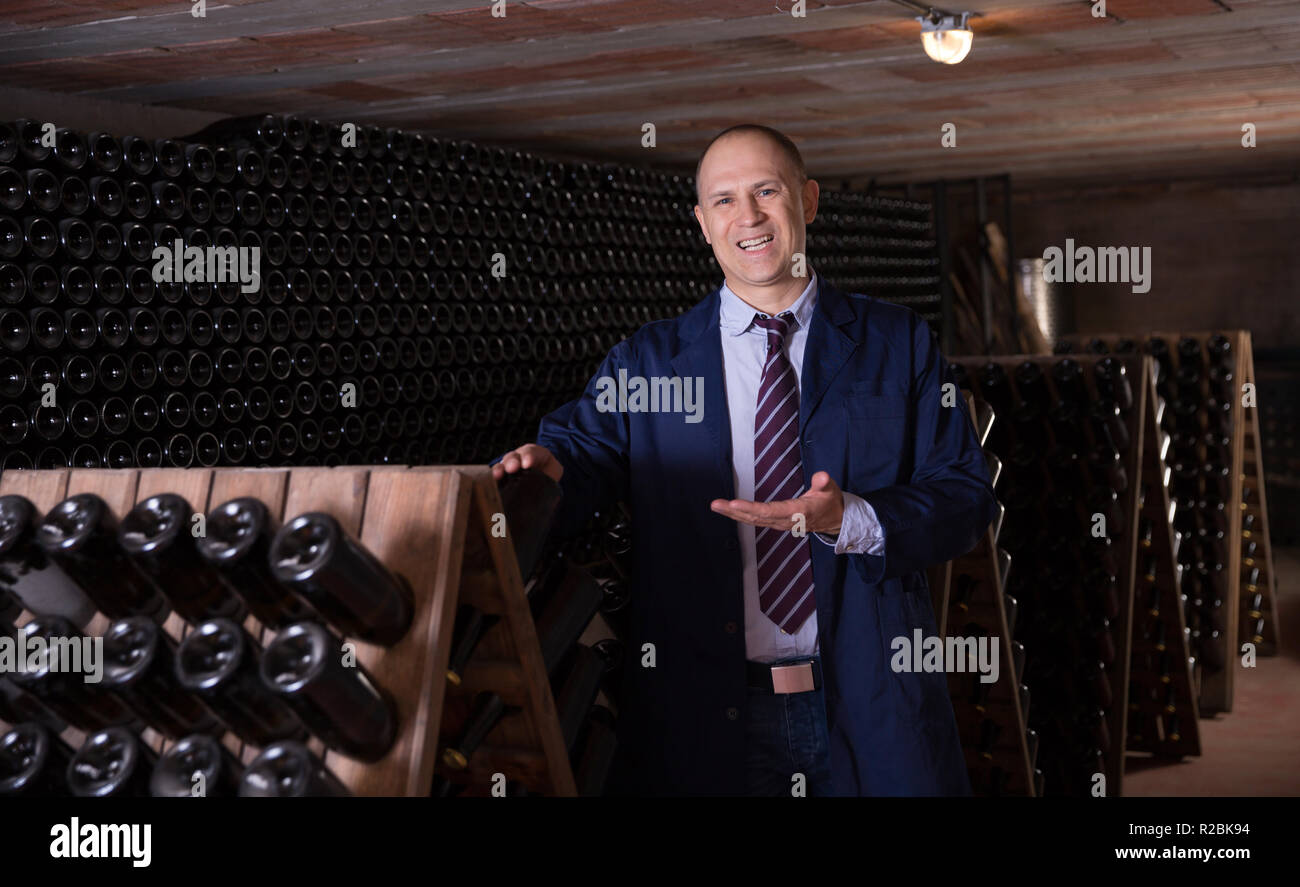 Male winemaker giving tour around winery, showing wine cellar with wine ...