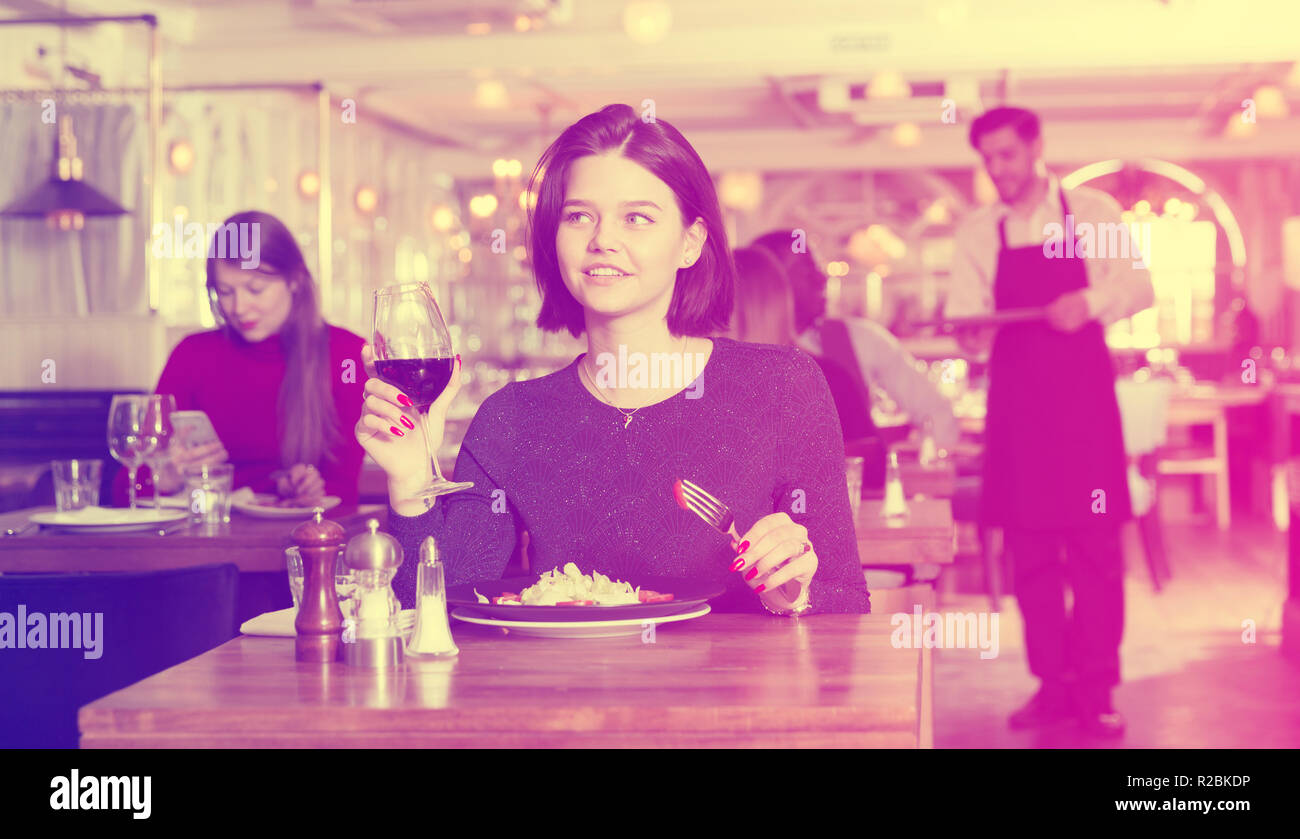 Happy girl enjoying delicious salad and red wine in stylish modern ...