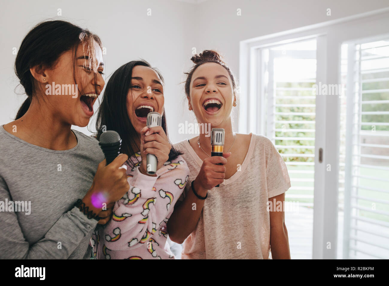 Three girls singing holding microphones standing in their room. Happy ...