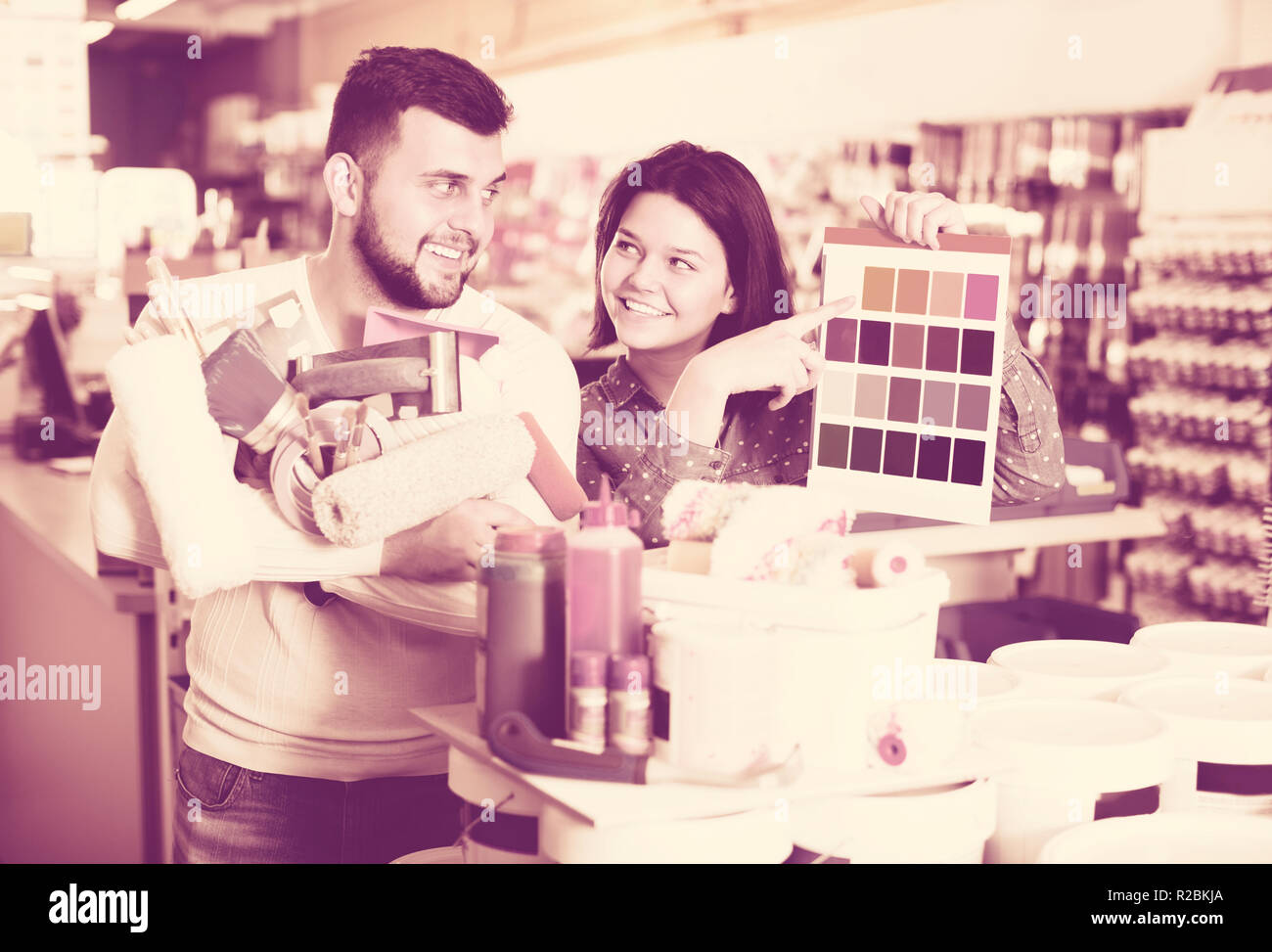 Young couple of customers checking color scheme in paint supplies shop ...