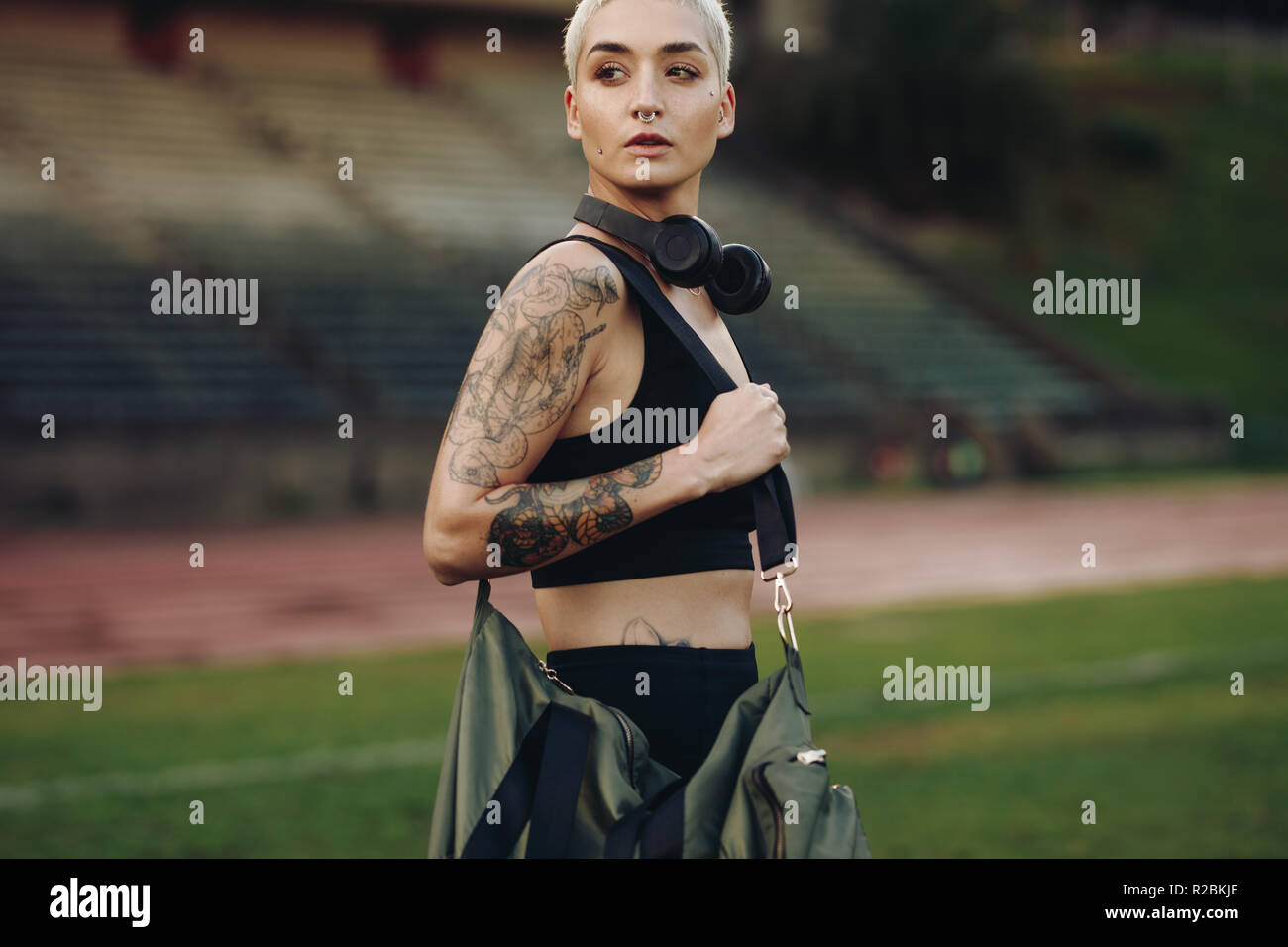 Female runner standing in a track and field stadium carrying her bag ...