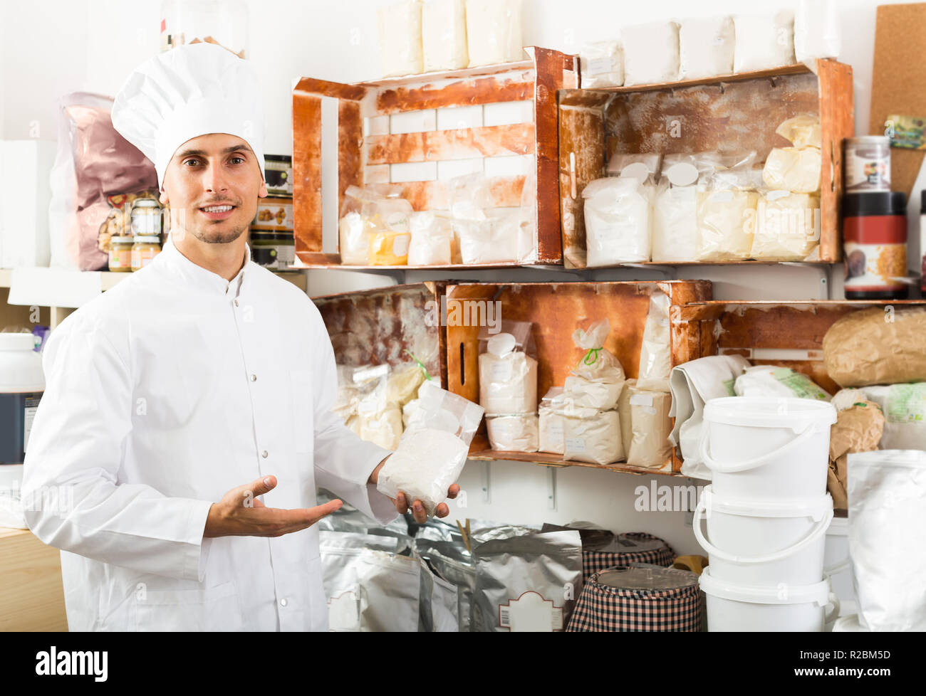 young man cook in white uniform taking package with grit in pantry room ...