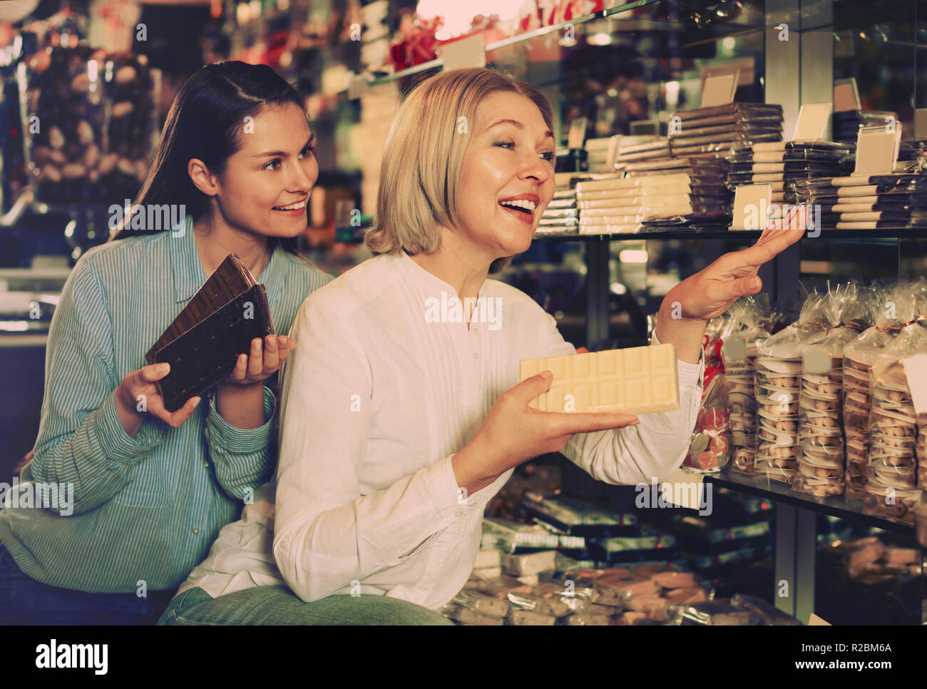 Ordinary female customers choosing delicious milk chocolate in shelf ...