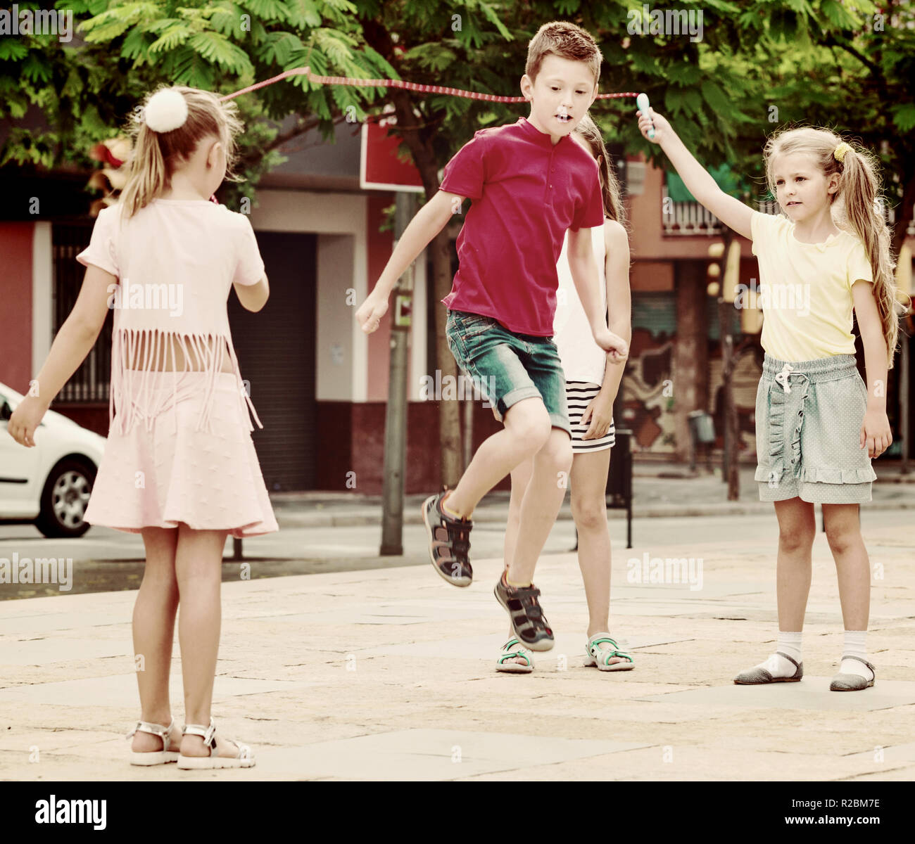 Smiling kids in school age playing together with jumping rope outdoors ...