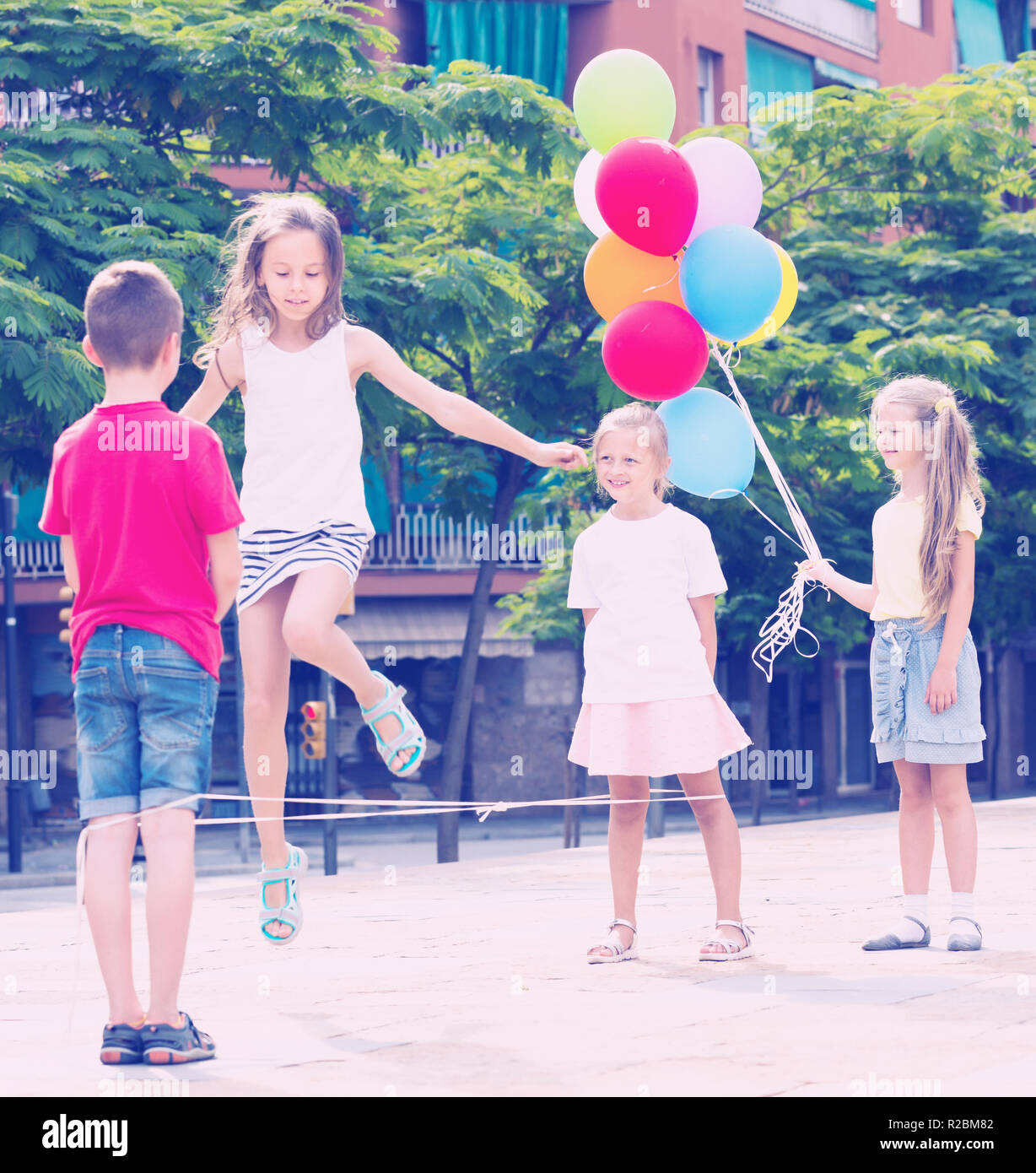 Cheerful kids in school age playing together with chinese jumping rope ...