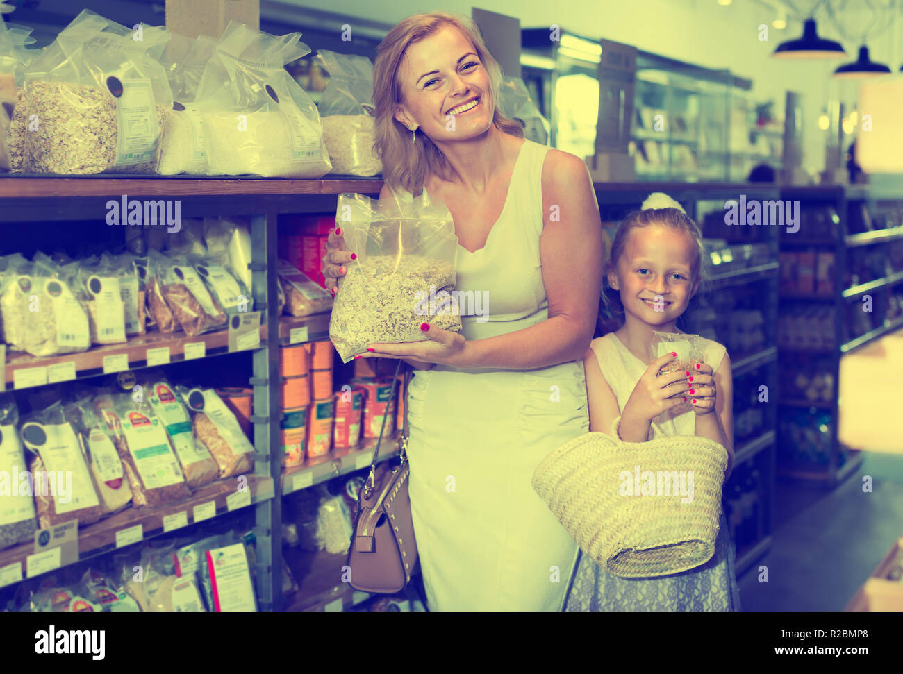 smiling blonde woman with little daughter buying various cereals in ...