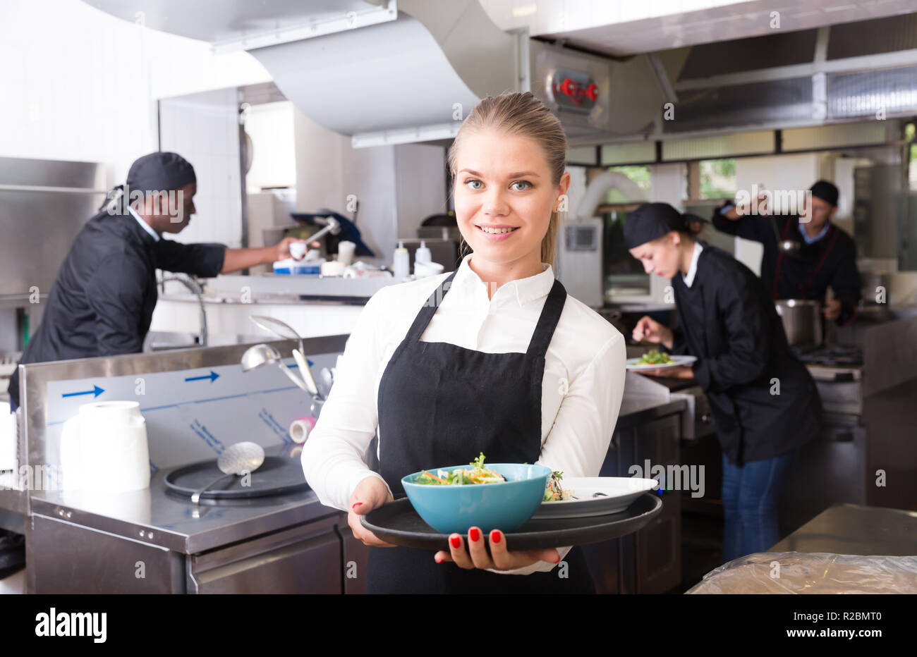 Successful young waitress standing in restaurant kitchen with ordered ...