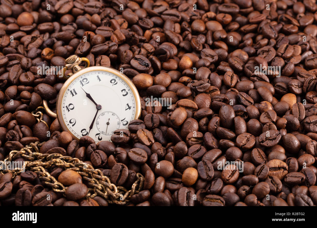 old pocket watch, golden, with a long chain on a pile of coffee beans ...