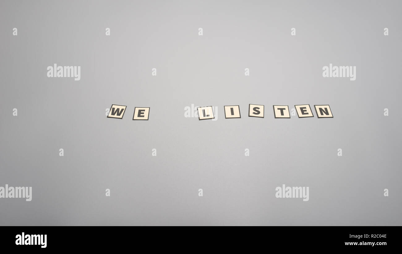 We listen sign assembled with paper cut letters over grey background ...