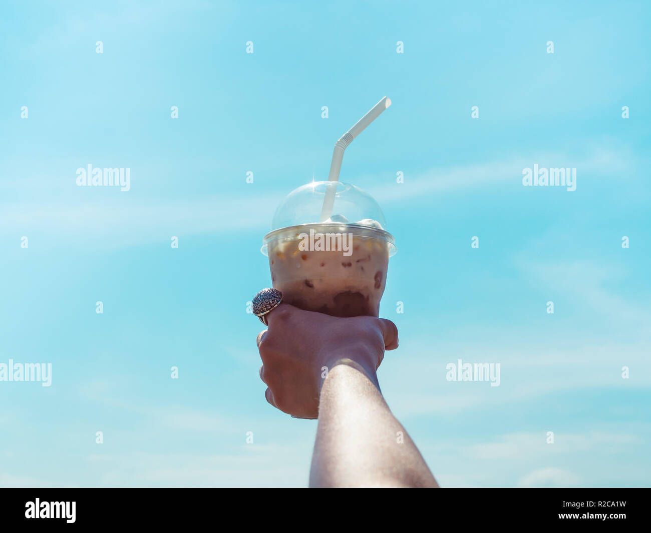 Hand with the ring on the finger holding a cup of iced coffee on blue ...